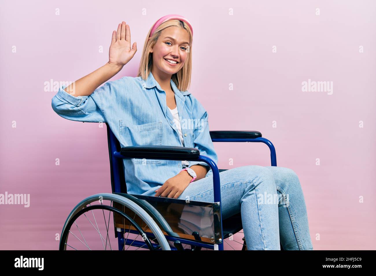 Beautiful blonde woman sitting on wheelchair waiving saying hello happy ...