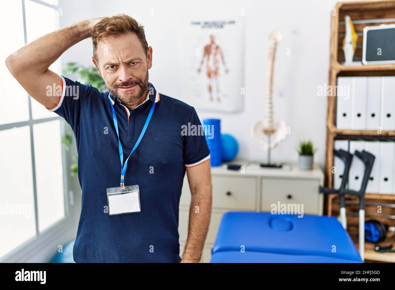 Middle age physiotherapist man working at pain recovery clinic confuse ...