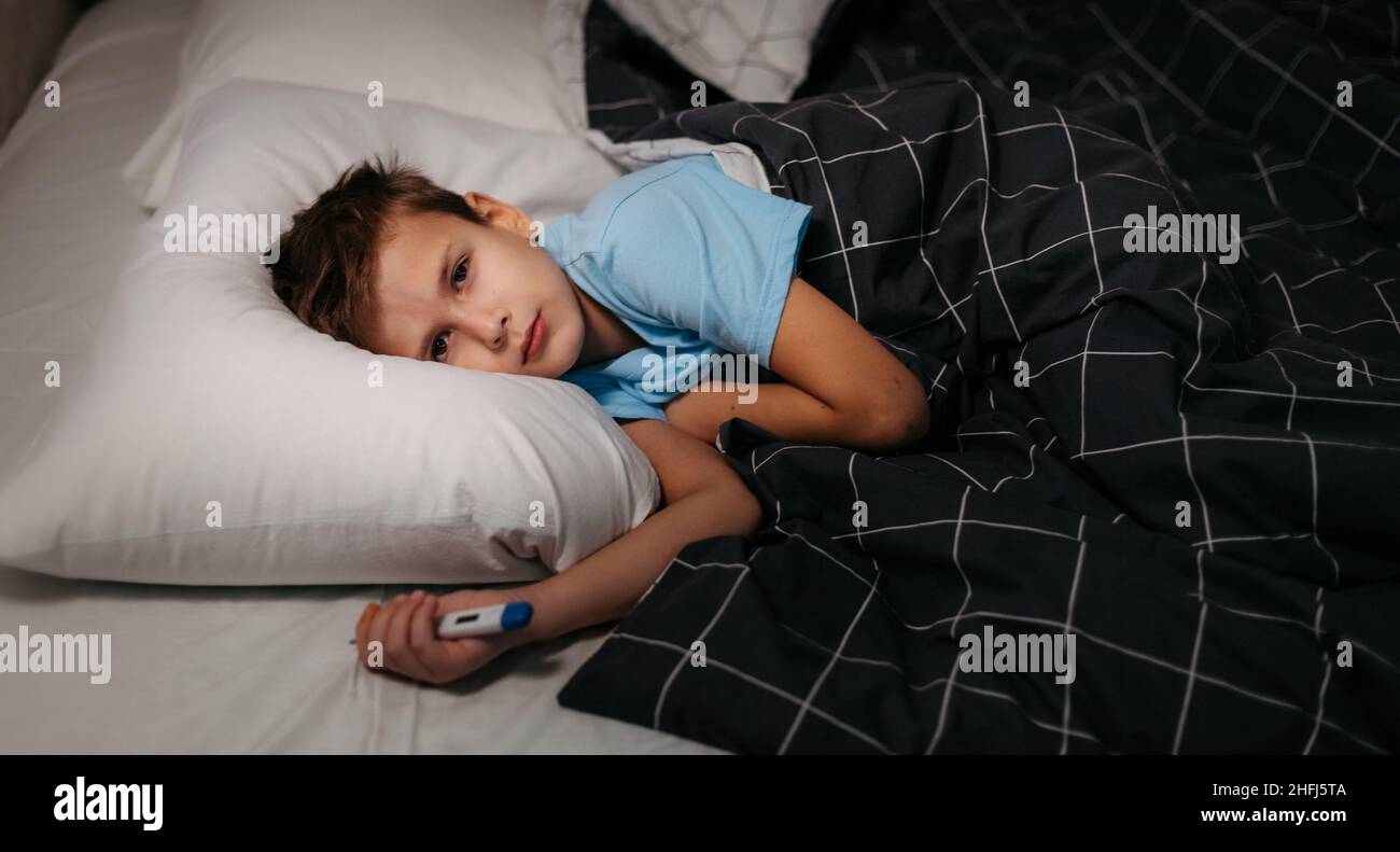 Sick child laying in bed and holding termometer Stock Photo - Alamy