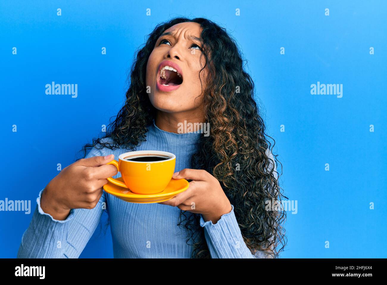 Young latin woman holding coffee angry and mad screaming frustrated and ...