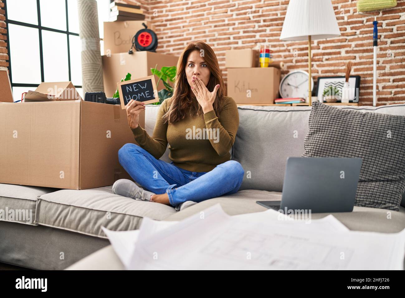 Hispanic woman moving to a new home covering mouth with hand, shocked ...
