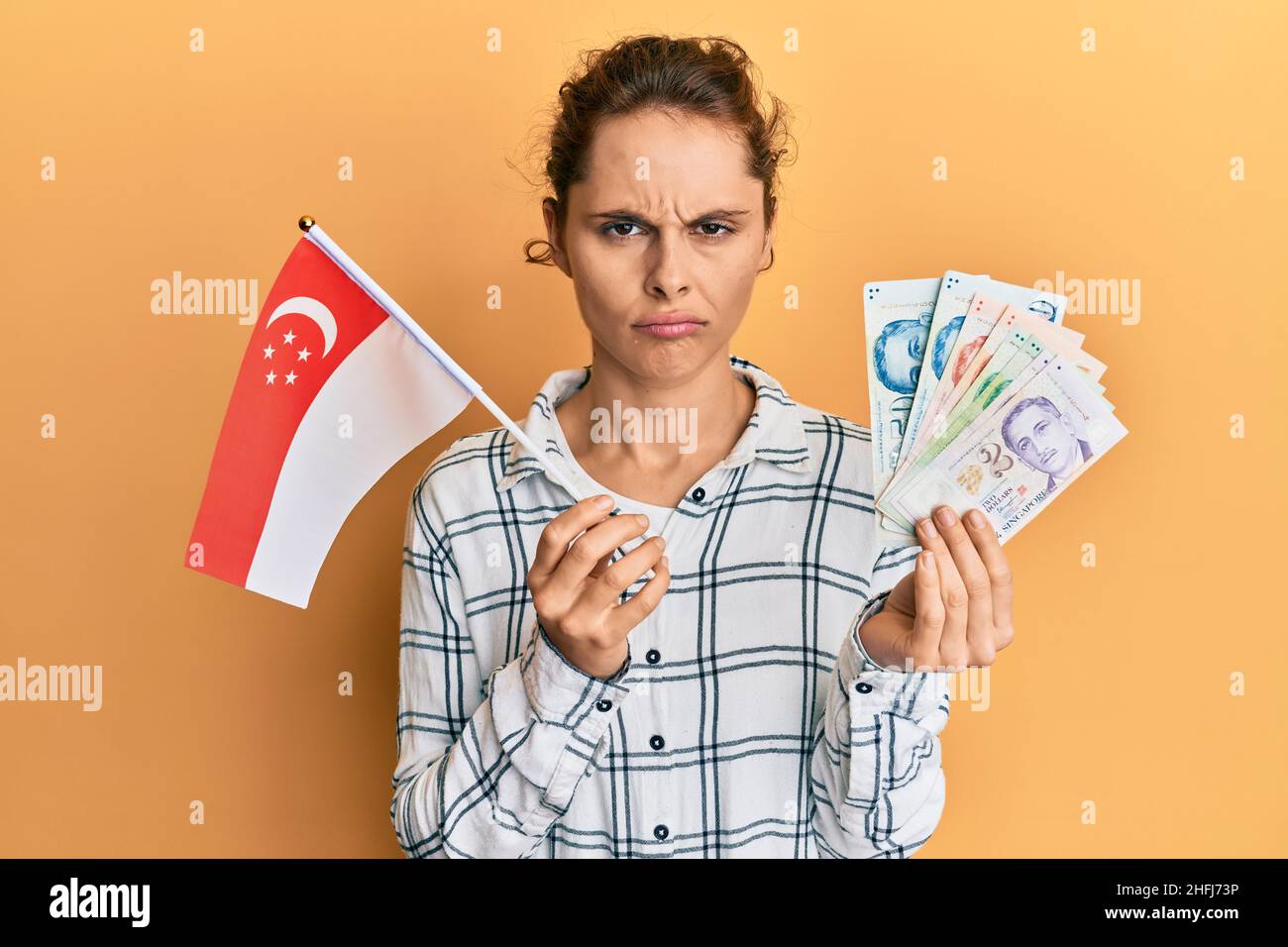 Young brunette woman holding singapore flag and dollars depressed and ...