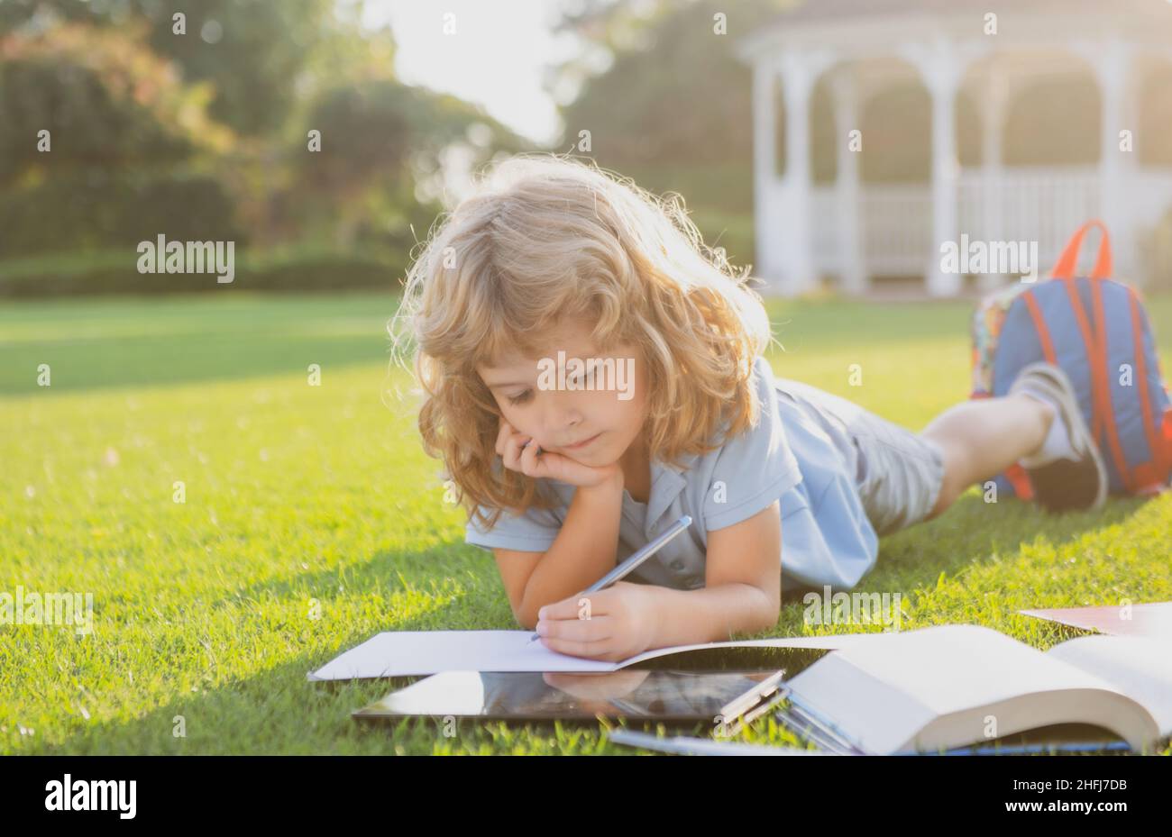 Beautiful child boy with book writing notes in copybook on grass ...