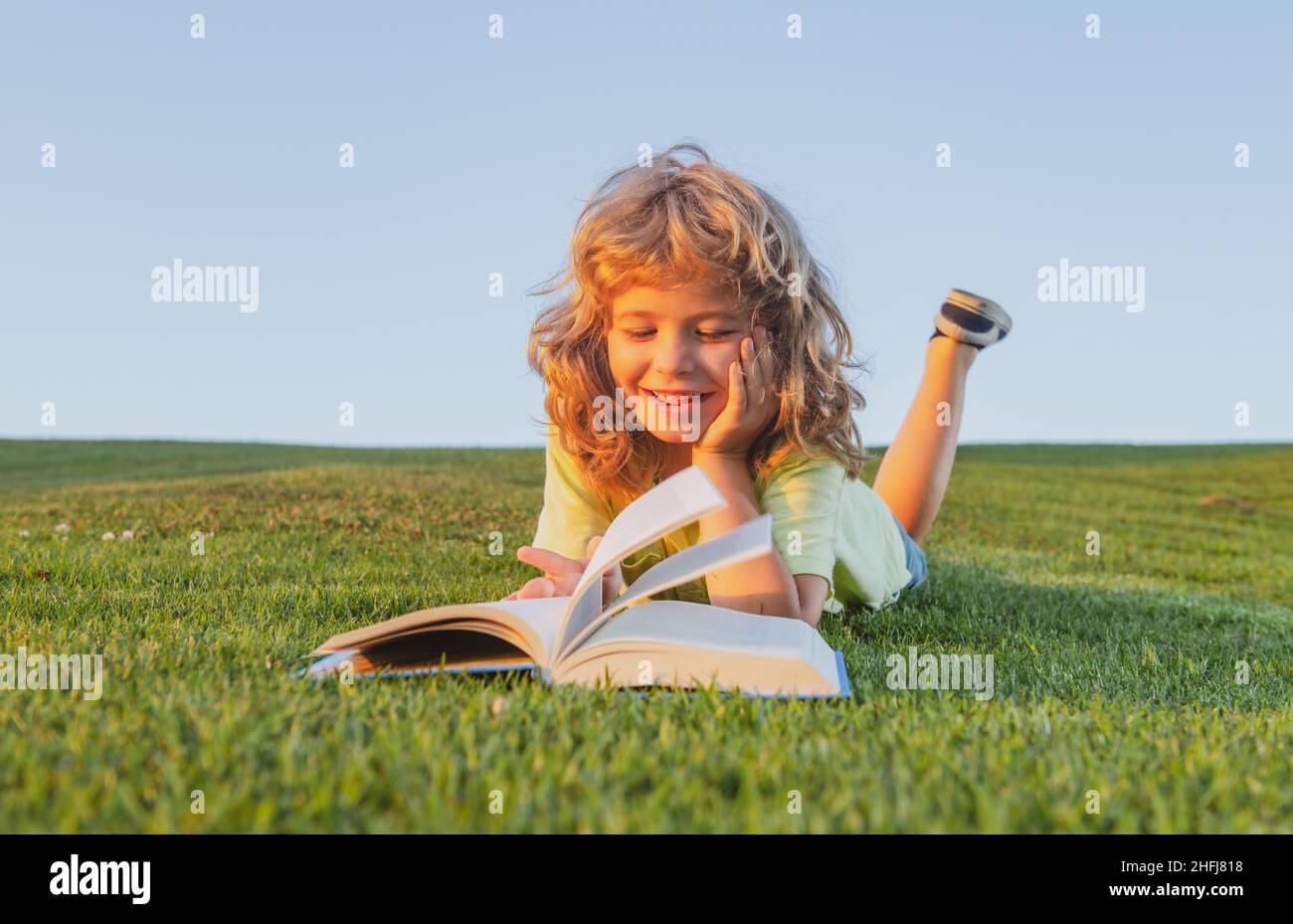 Funny kid reading the book in spring park. Child boy reading book ...