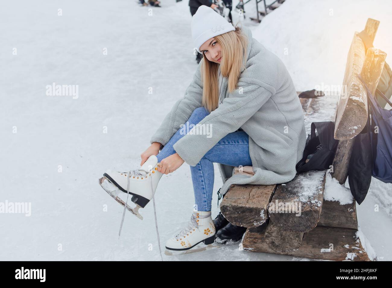 Lovely young woman sitting on the bench and puting on figure skates on ...