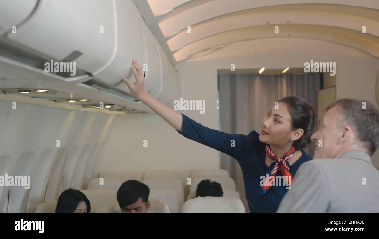Flight attendant woman service helping businessman passenger to put ...