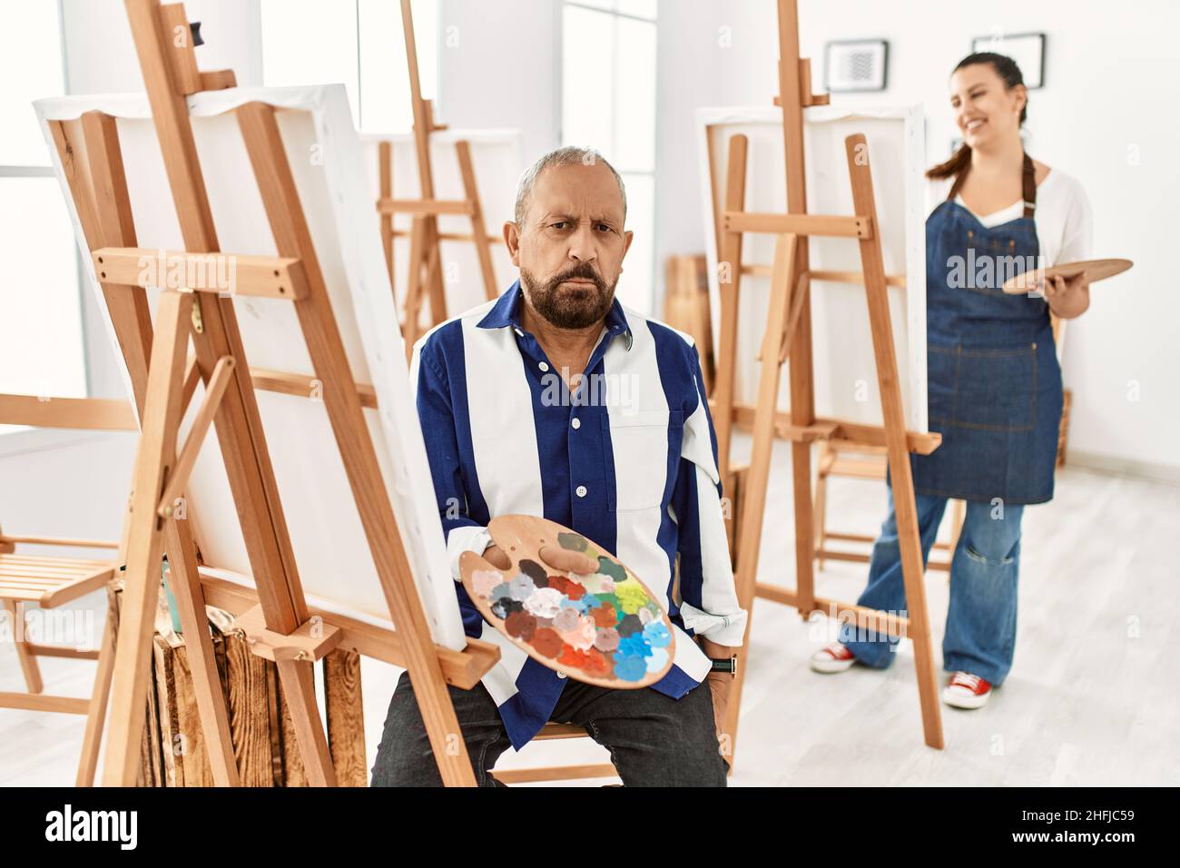 Senior artist man at art studio skeptic and nervous, frowning upset ...