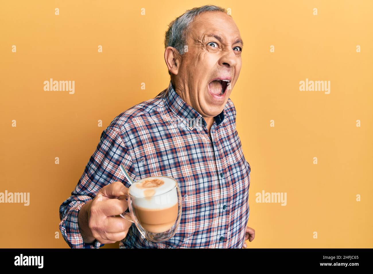 Handsome senior man with grey hair drinking a cup coffee angry and mad ...