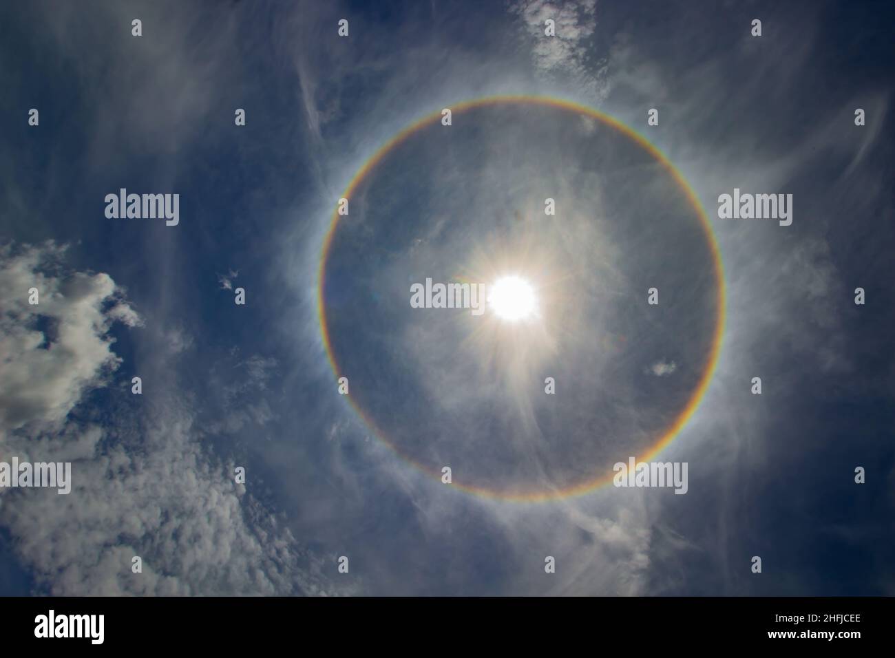 circular rainbow halo around the sun among blue sky and white clouds ...