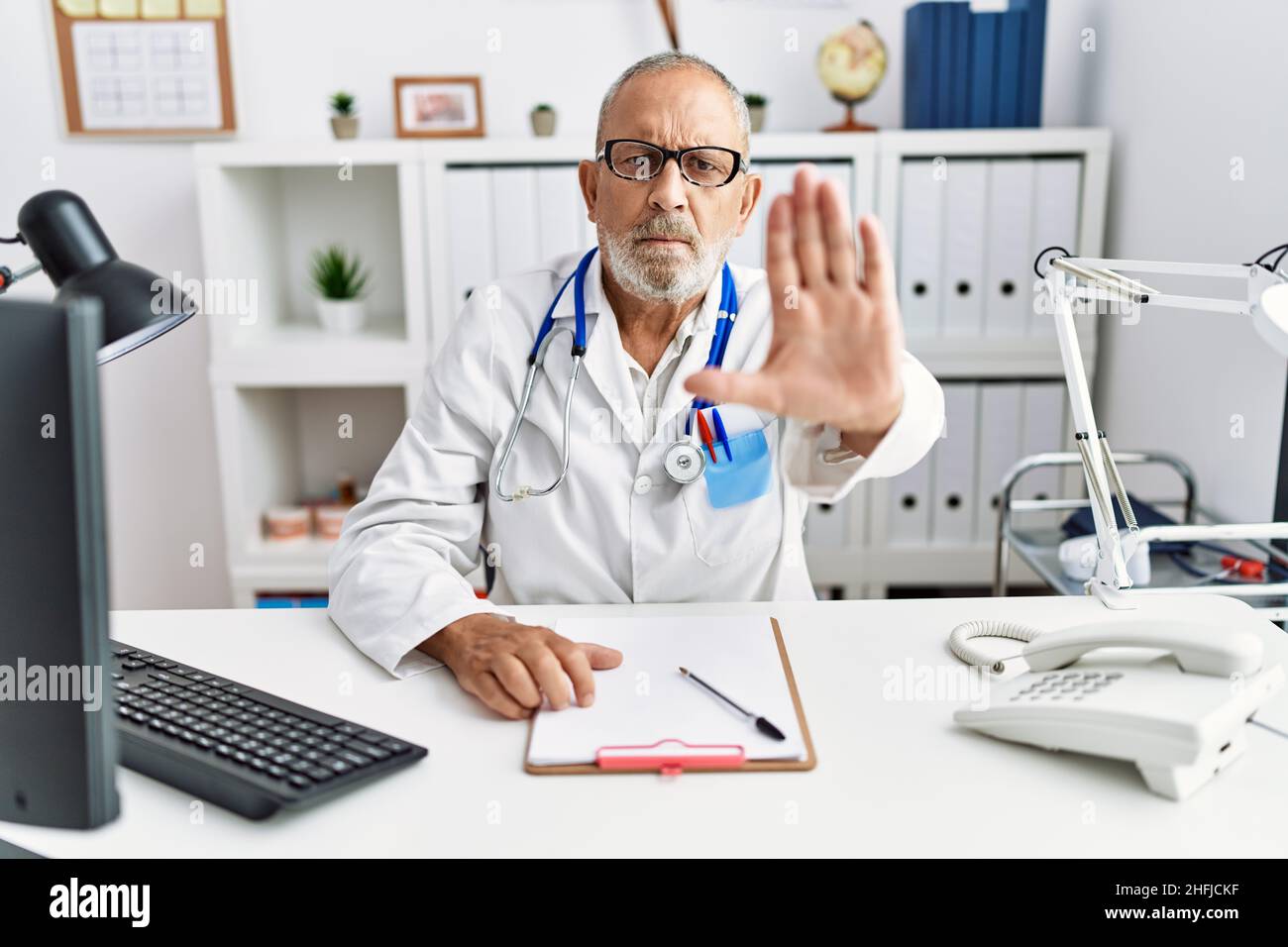 Mature doctor man at the clinic doing stop sing with palm of the hand ...