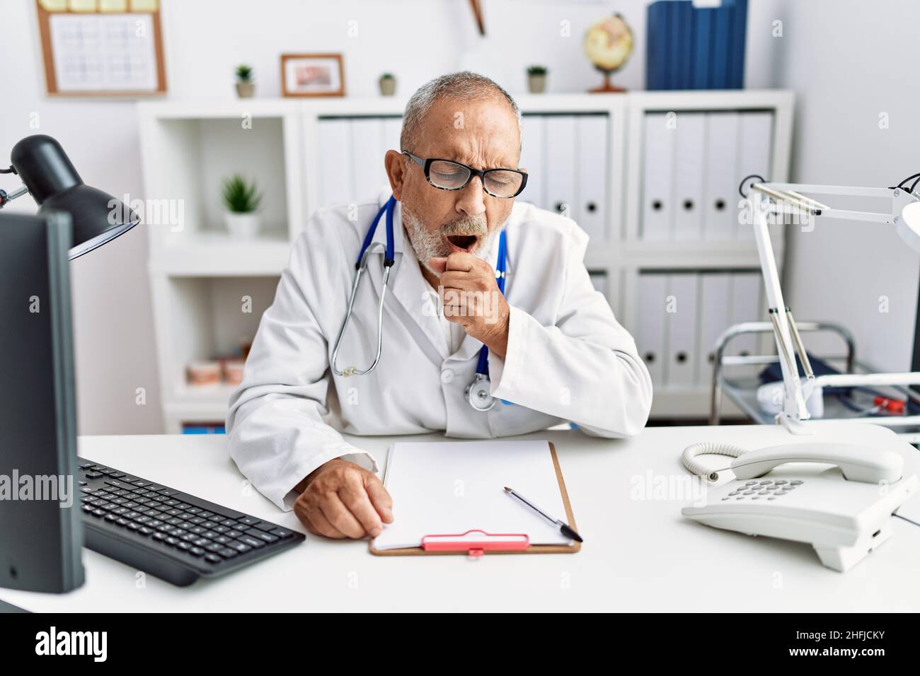 Mature doctor man at the clinic feeling unwell and coughing as symptom ...