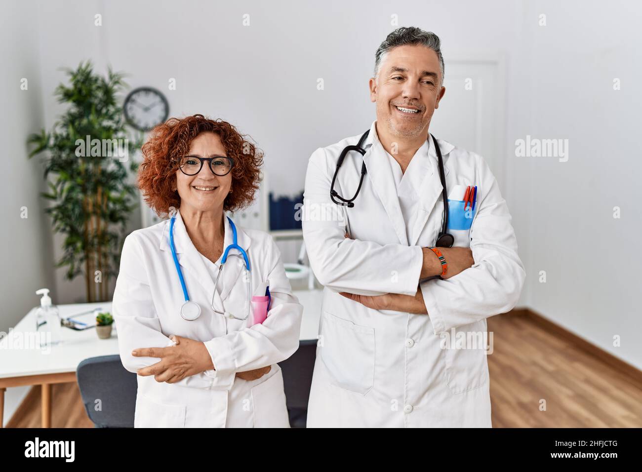 Two middle age doctors at medical clinic happy face smiling with ...