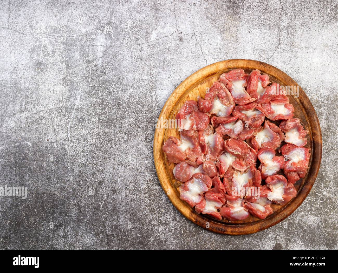 Raw chicken gizzards on a round wooden cutting board on a dark grey ...