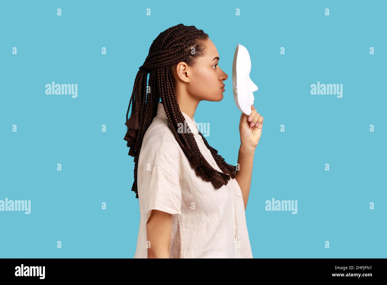 Side view portrait of woman with black dreadlocks holding white mask in ...