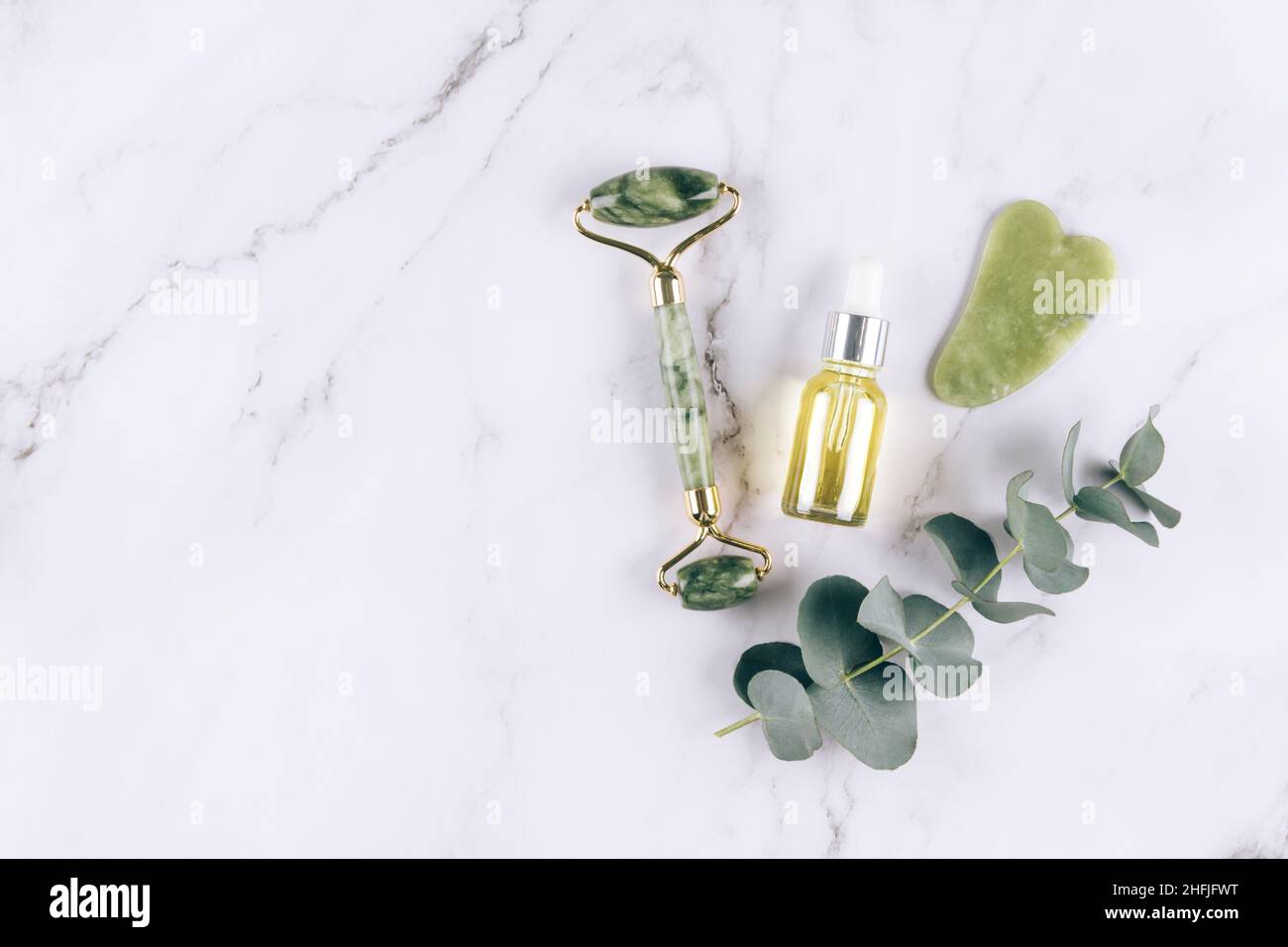 Flat lay with jade facial roller and gua sha tool with beauty serum and ...
