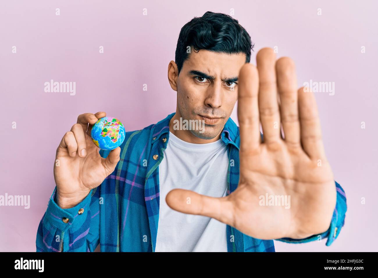 Handsome hispanic man holding small world ball with open hand doing ...