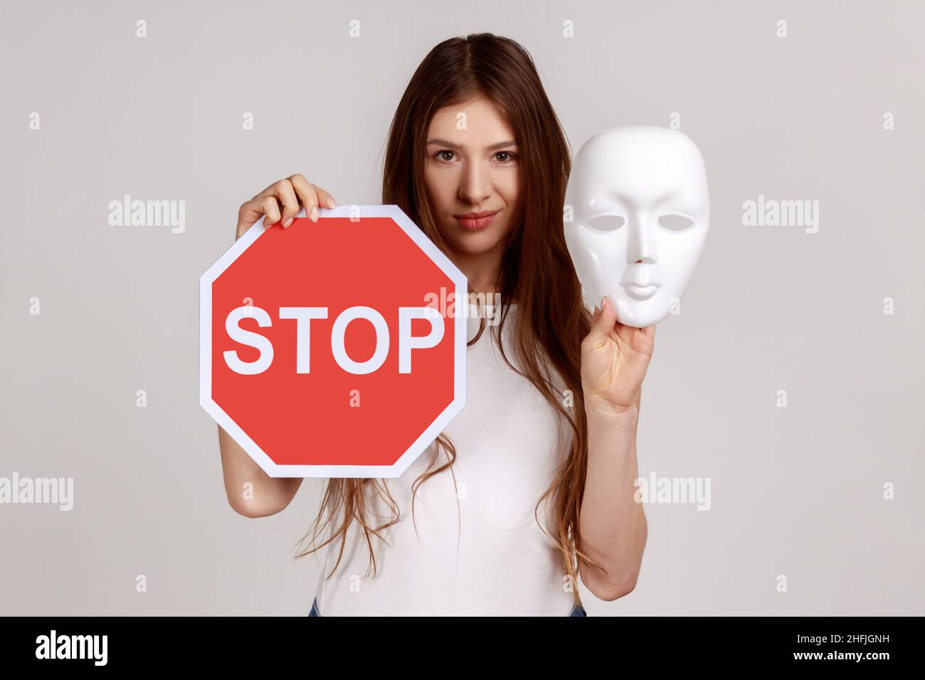 Portrait of serious dark haired woman holding white mask with unknown ...