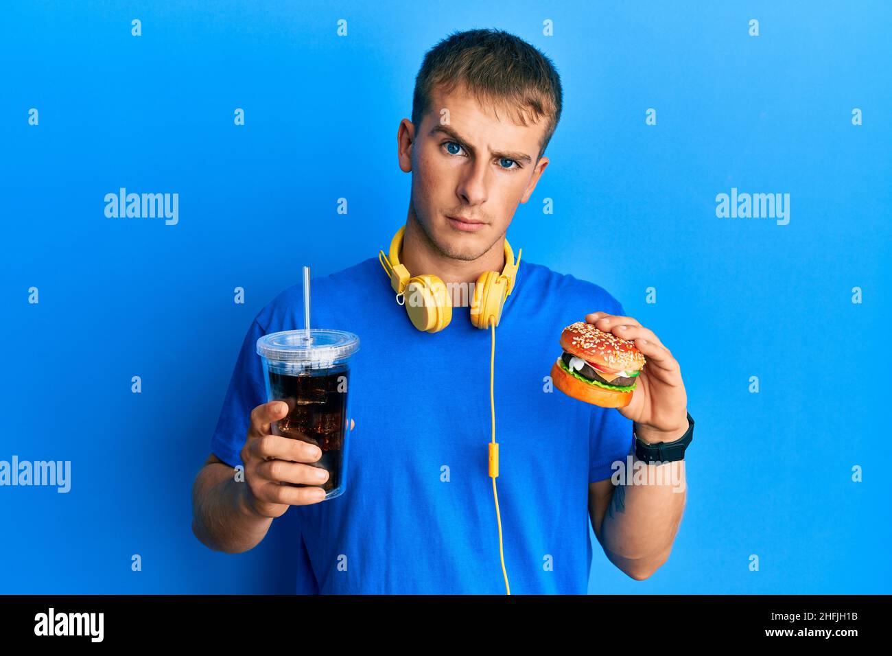 Young caucasian man eating a tasty classic burger and soda skeptic and ...