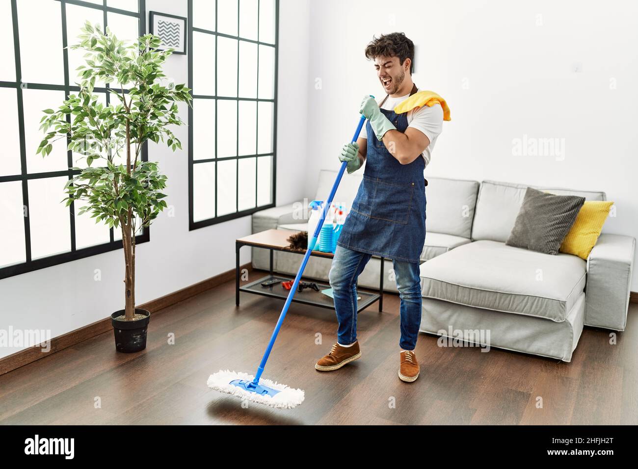 Young hispanic man doing chores singing using mop as a microphone at ...