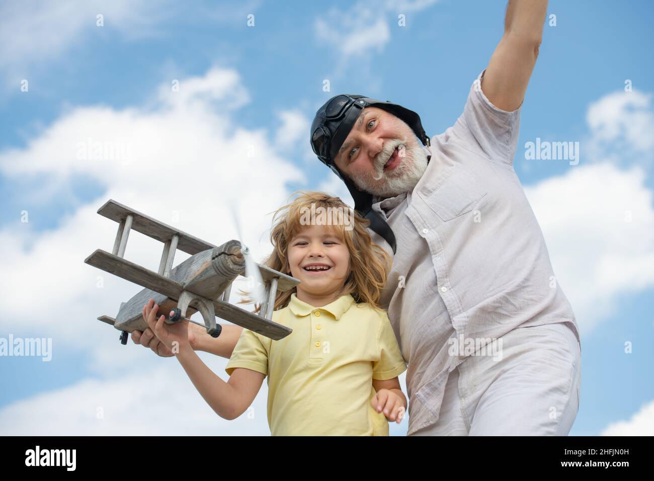 Funny grandson child and grandfather playing with wooden plane against ...