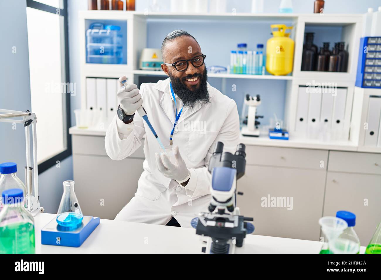 Young african american man wearing scientist uniform using pipette at ...