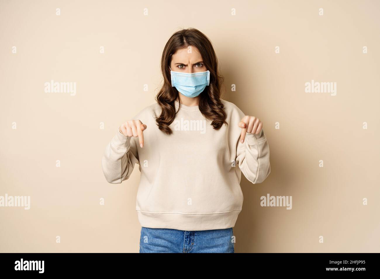 Angry woman in medical face mask, pointing fingers down and looking ...