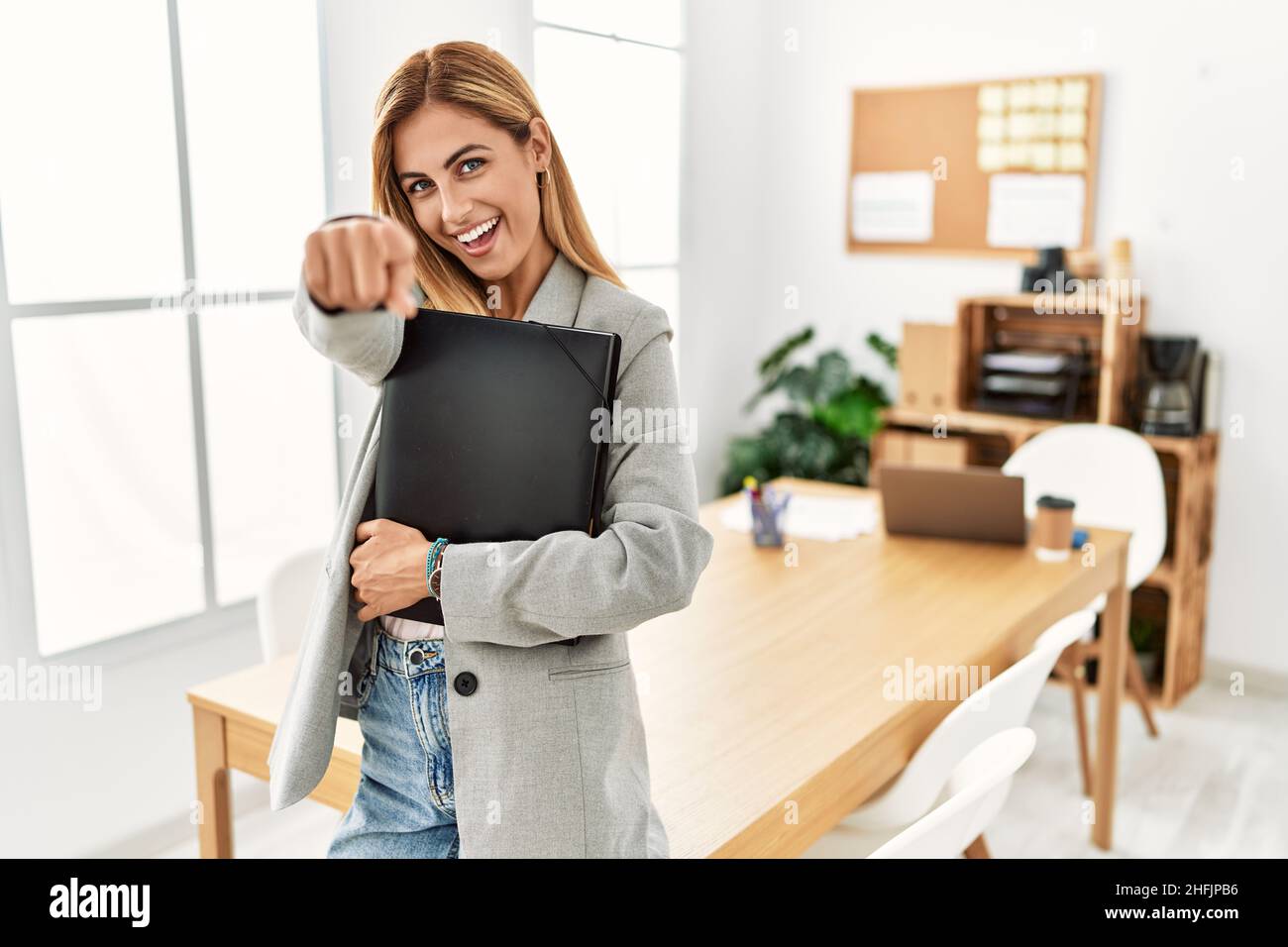 Blonde business woman at the office pointing to you and the camera with ...