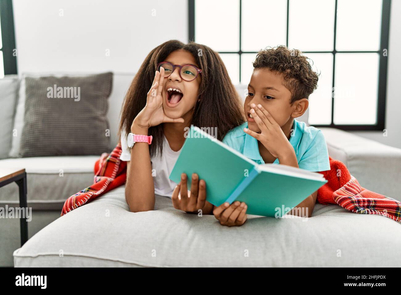Two siblings lying on the sofa reading a book shouting and screaming ...