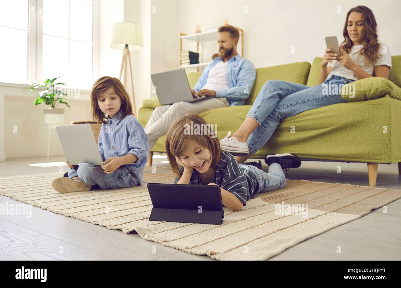 Boy lying on floor with tablet while mom, dad and brother are using ...