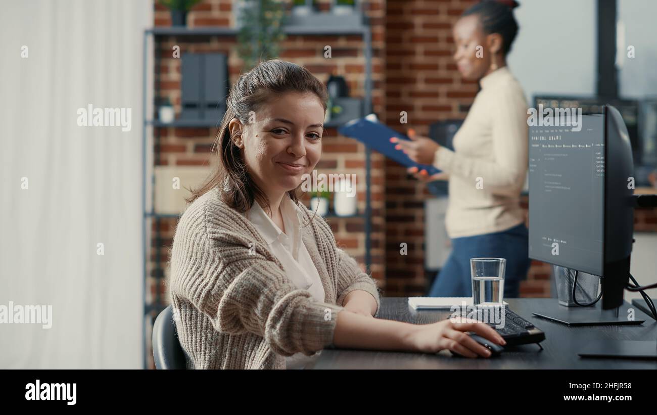 Programer typing source code on computer keyboard turning head and smiling at camera. Casual ...