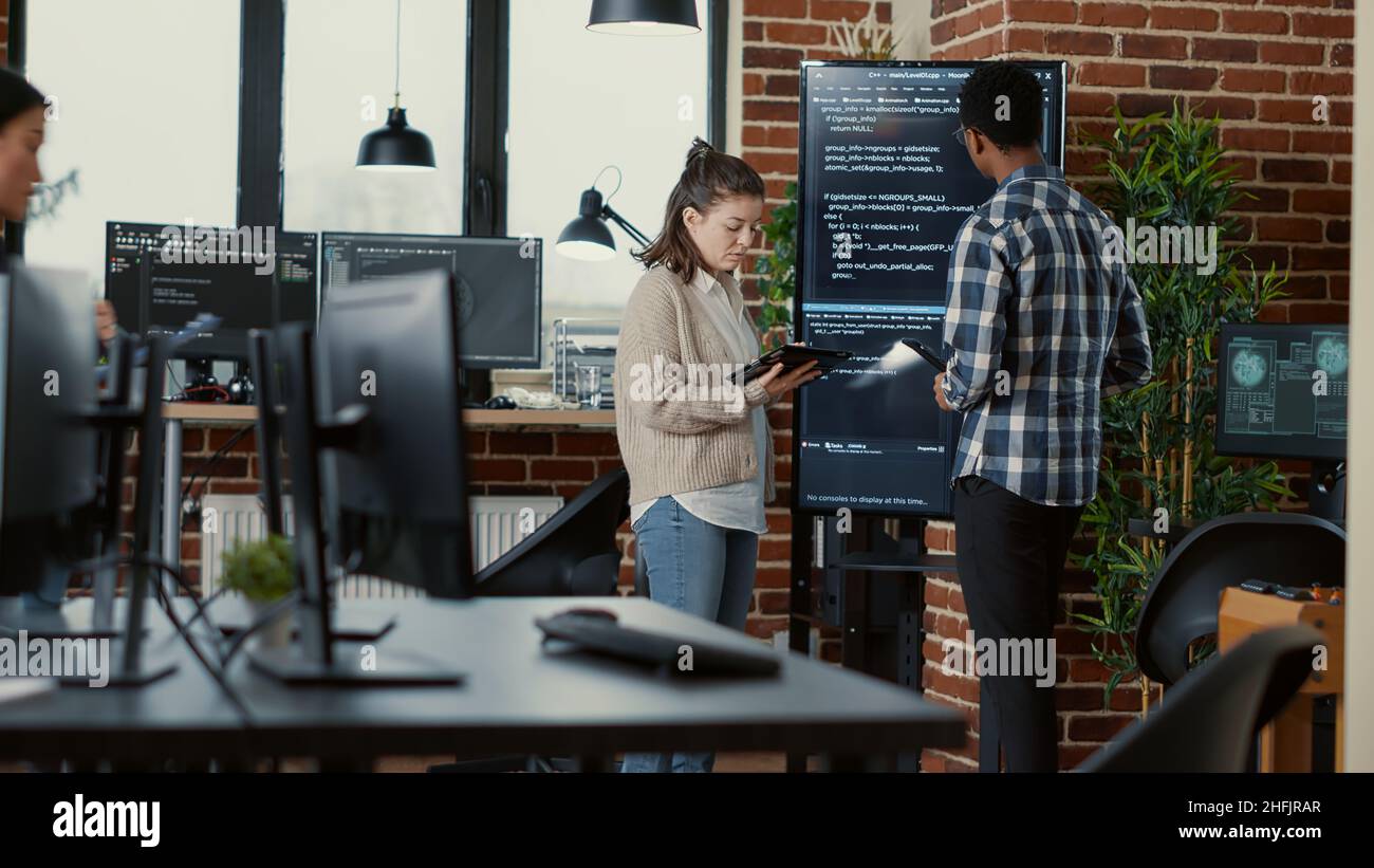 Software Developer Holding Digital Tablet Analyzing Code On Wall Screen Tv Explaining Errors To