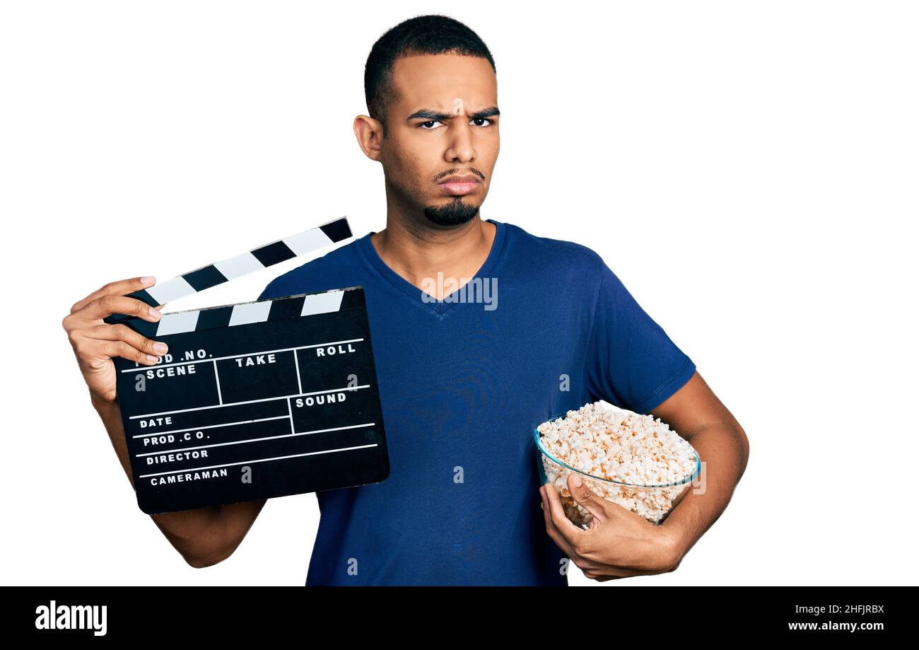 Young african american man eating popcorn holding film clapboard ...