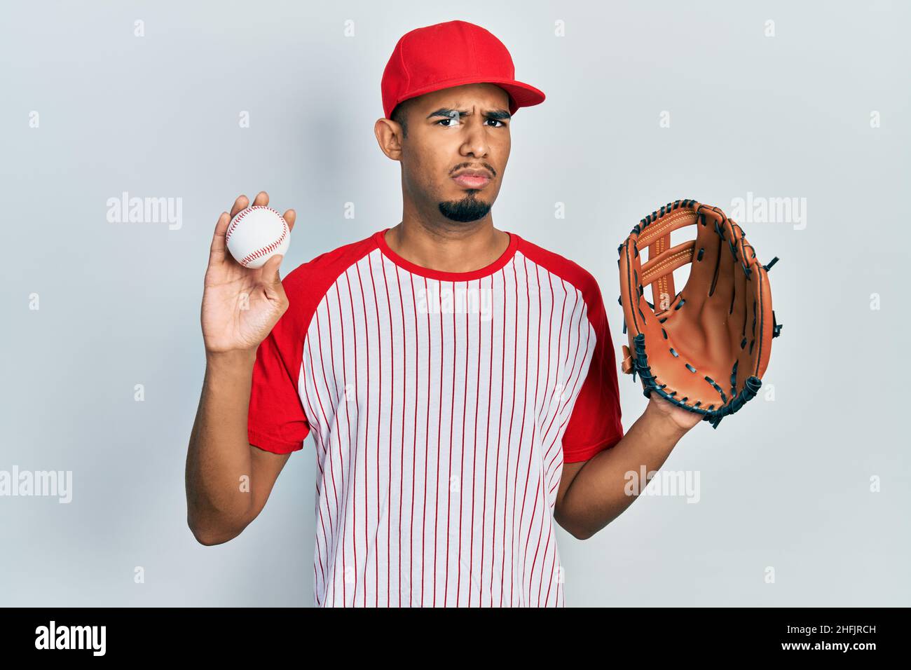 Young african american man wearing baseball uniform holding glove and ...