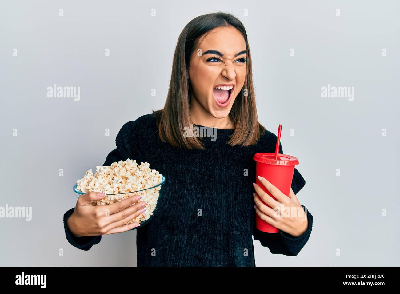 Young brunette girl eating popcorn and drinking soda angry and mad ...