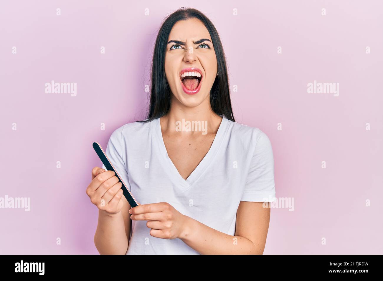 Beautiful woman with blue eyes using file nail angry and mad screaming ...