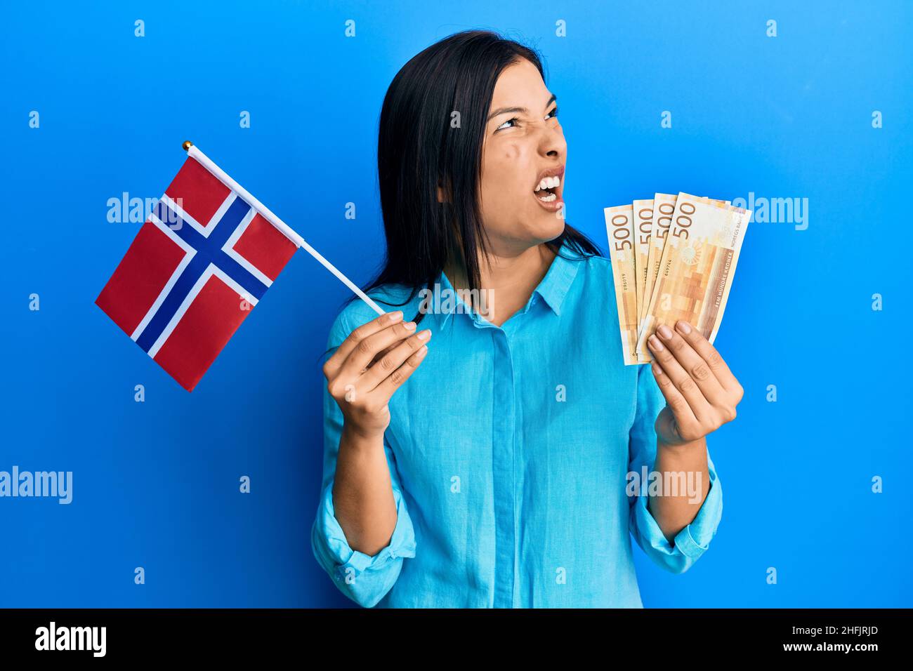 Young latin woman holding norway flag and krone banknotes angry and mad ...