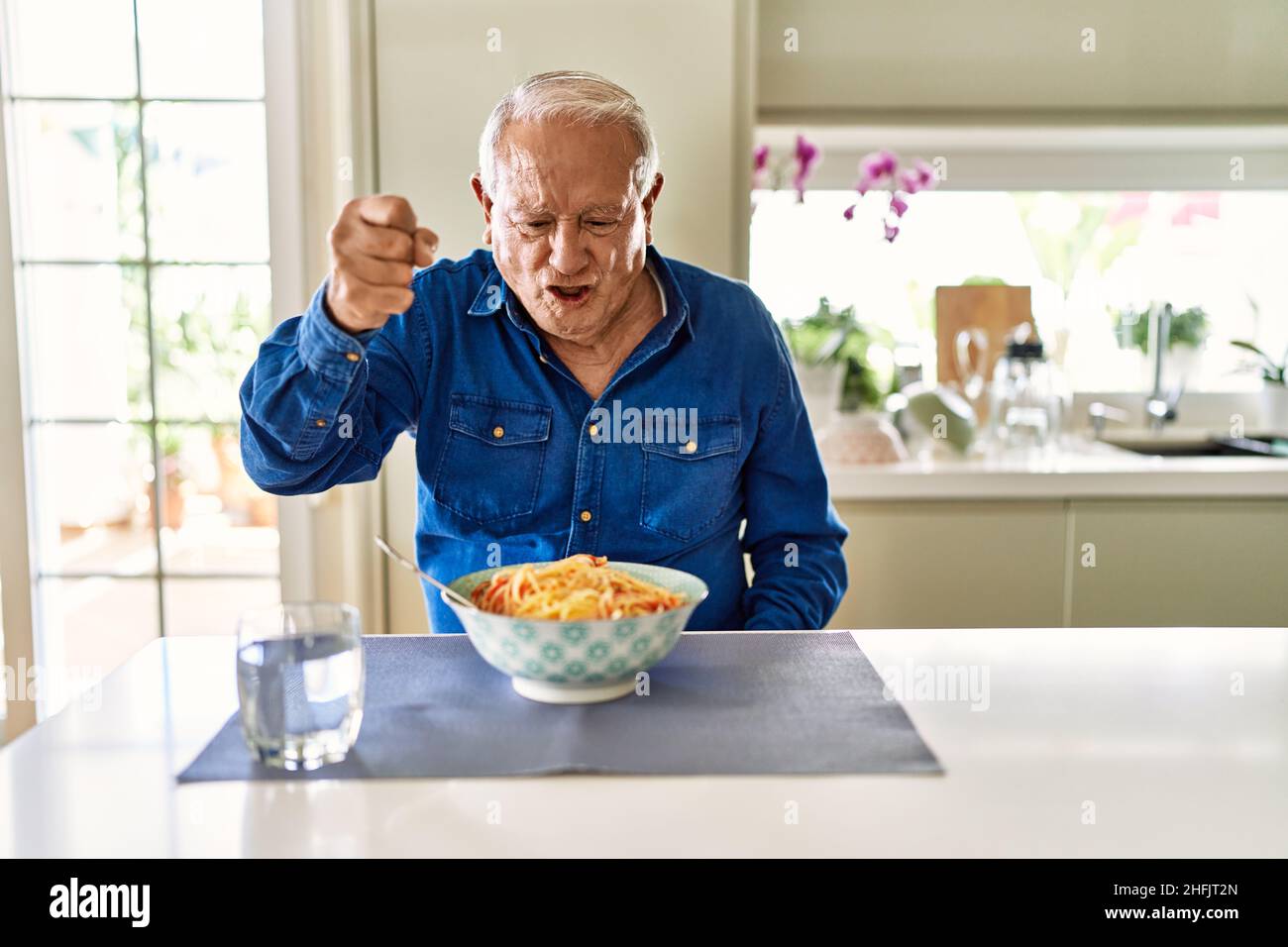 Senior man with grey hair eating pasta spaghetti at home angry and mad ...