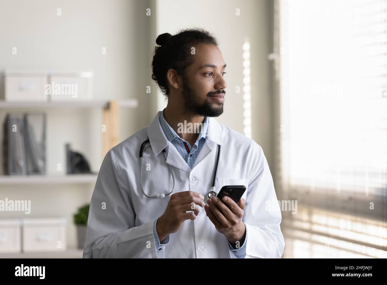 Happy dreamy young African American doctor holding cellphone Stock ...
