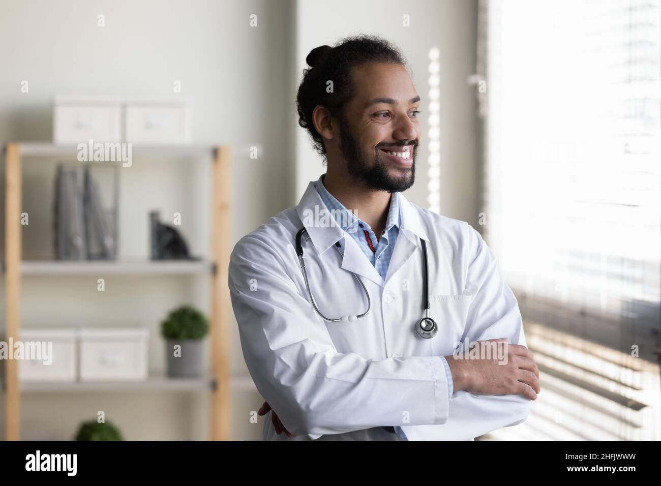 Happy dreamy young African American male doctor standing in office ...