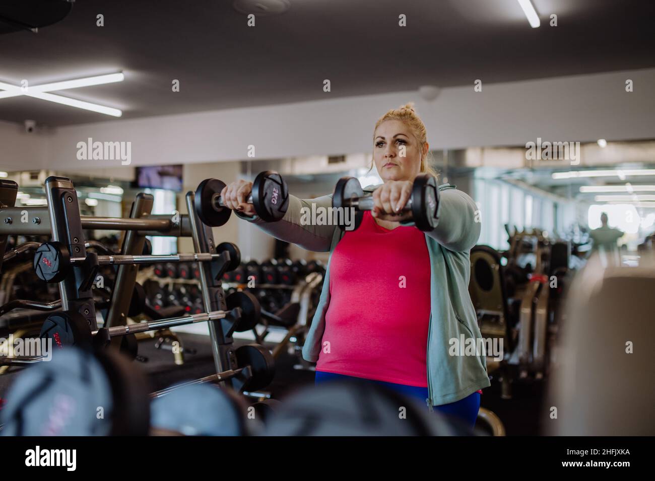 Plus size woman training and lifting dumbbells indoors in gym Stock ...
