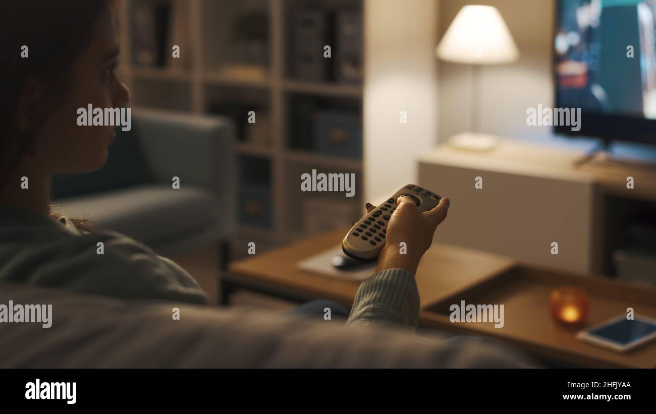 Woman sitting on the couch in the living room and watching TV, she is ...