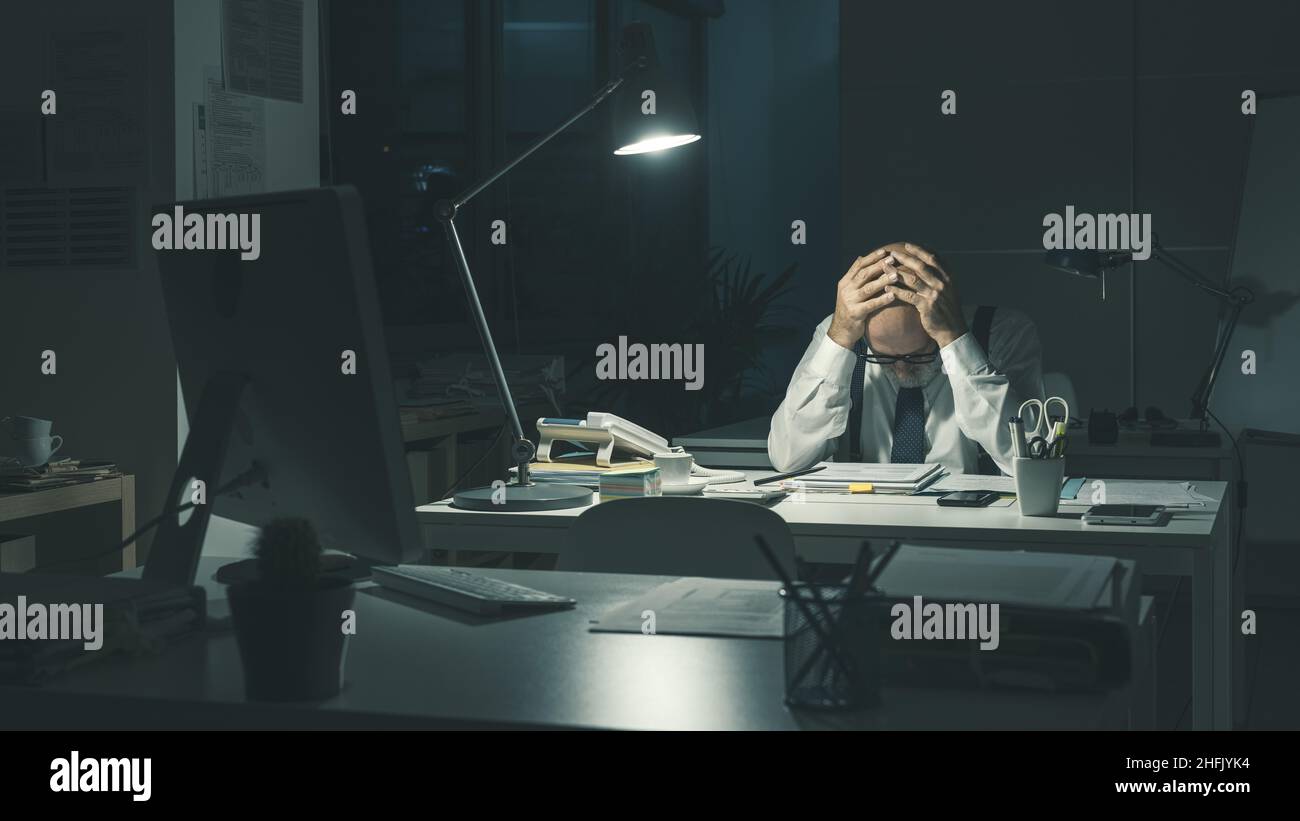 Stressed business executive sitting at desk and working overtime at ...