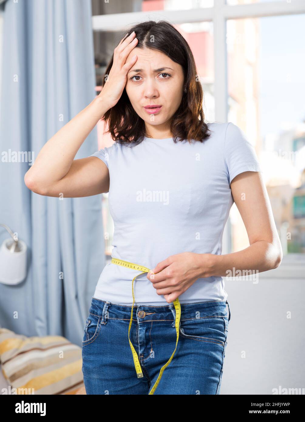 Sad young woman measuring waist with measuring tape Stock Photo - Alamy