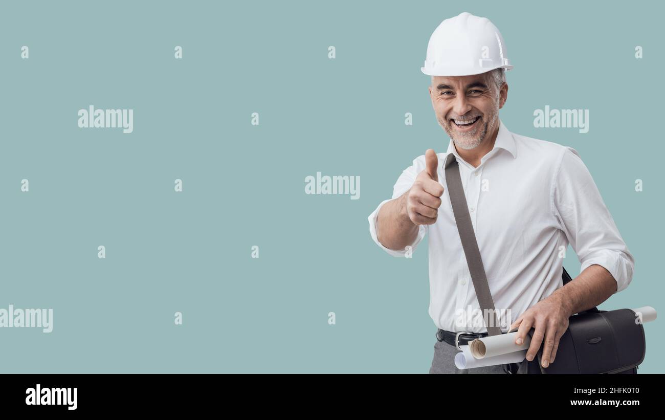 Cheerful construction engineer giving a thumbs up and carrying paper ...