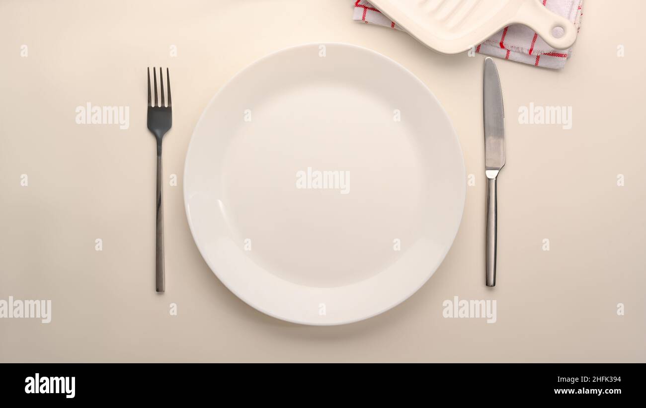 Empty simple white ceramic plate with silverware on white table, top ...
