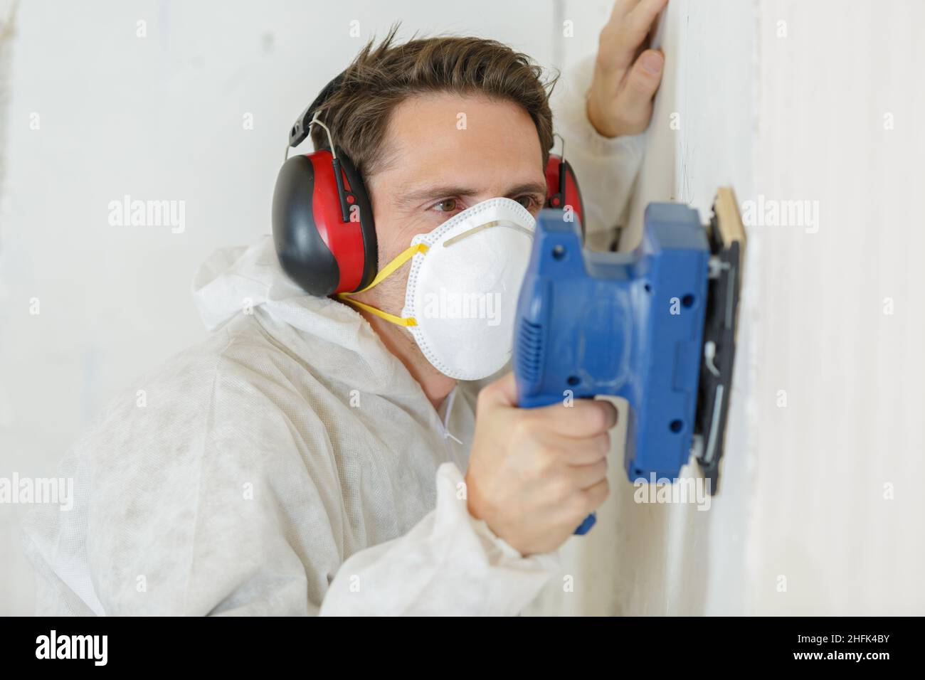 man sanding a wall with a power sander Stock Photo - Alamy