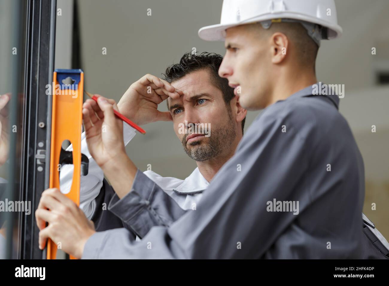 apprentice using spirit level supervisor watching and frowning Stock ...