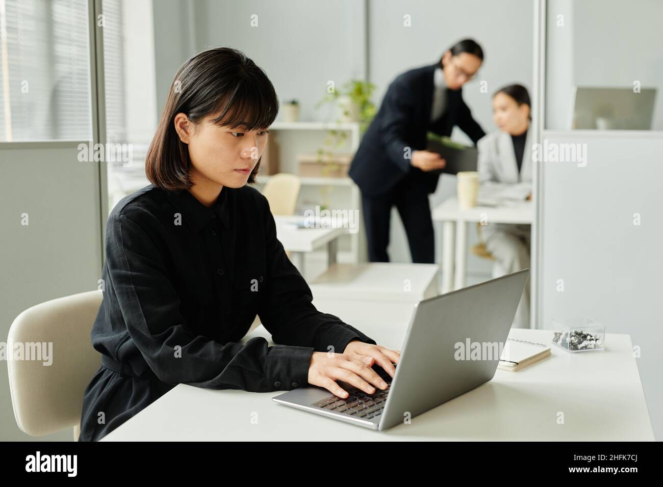 Side view portrait of young woman using laptop while working at desk in ...