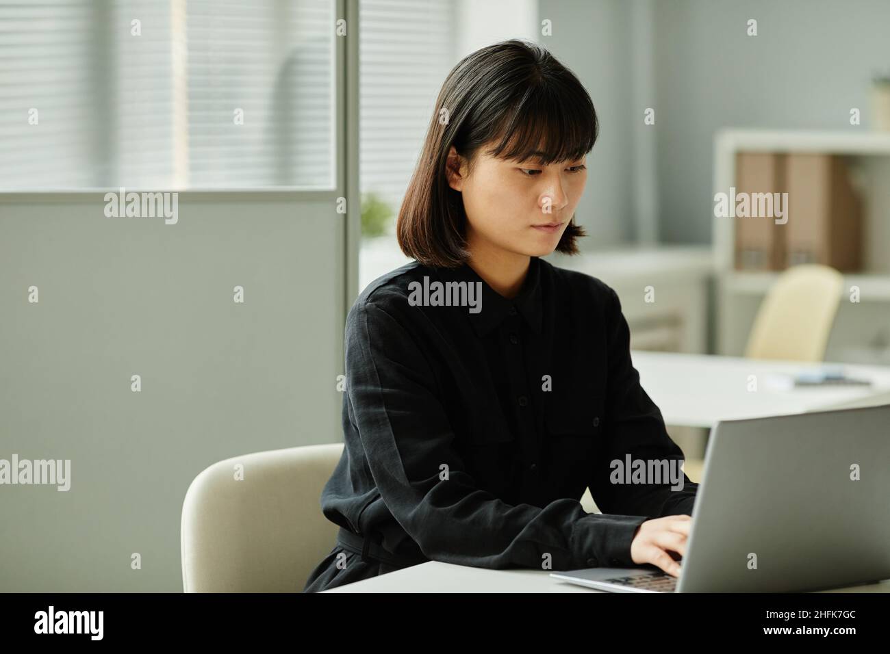 Minimal portrait of young woman using laptop while working at desk in ...