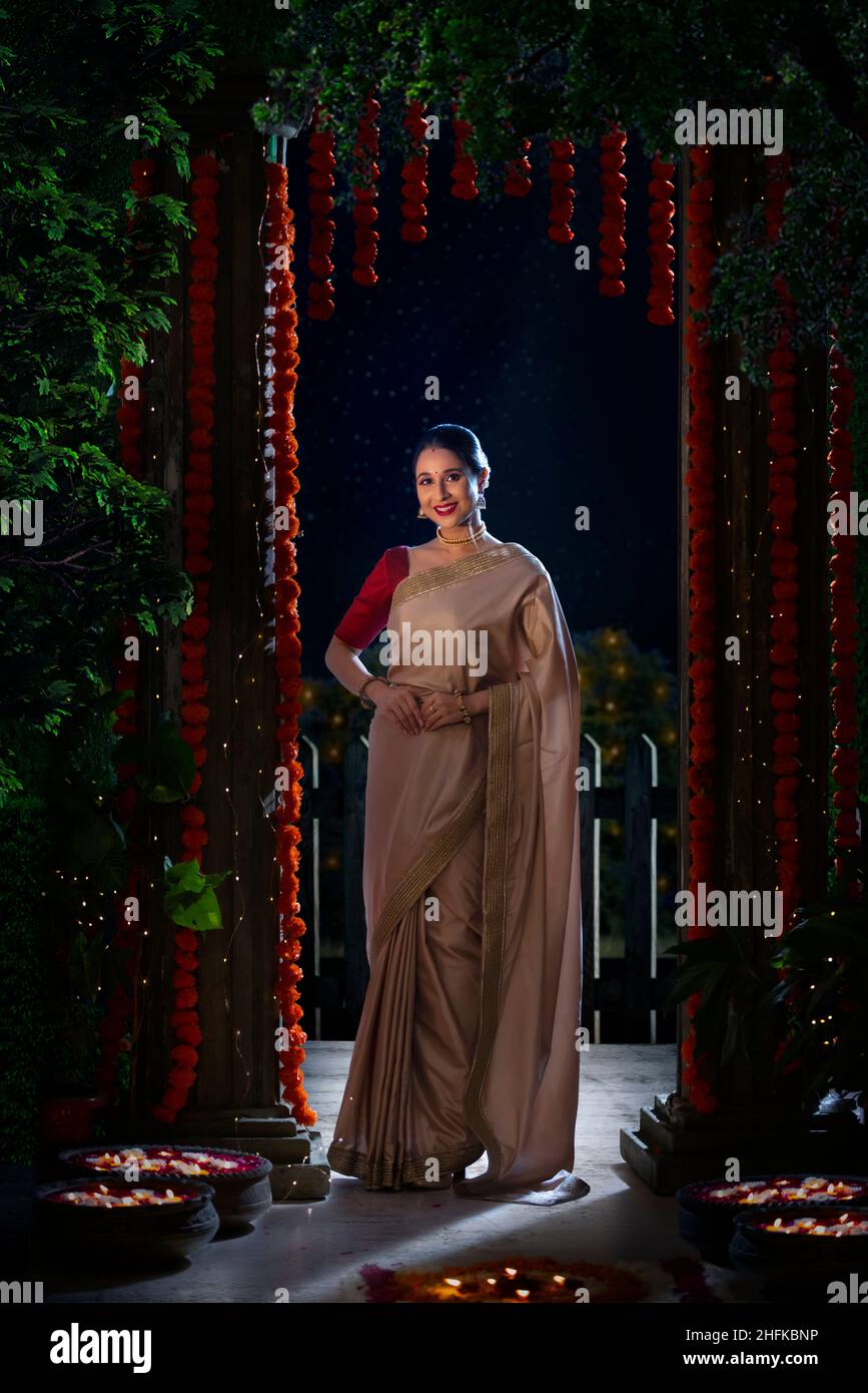 Beatiful Indian woman in golden saree standing at outdoor gate ...